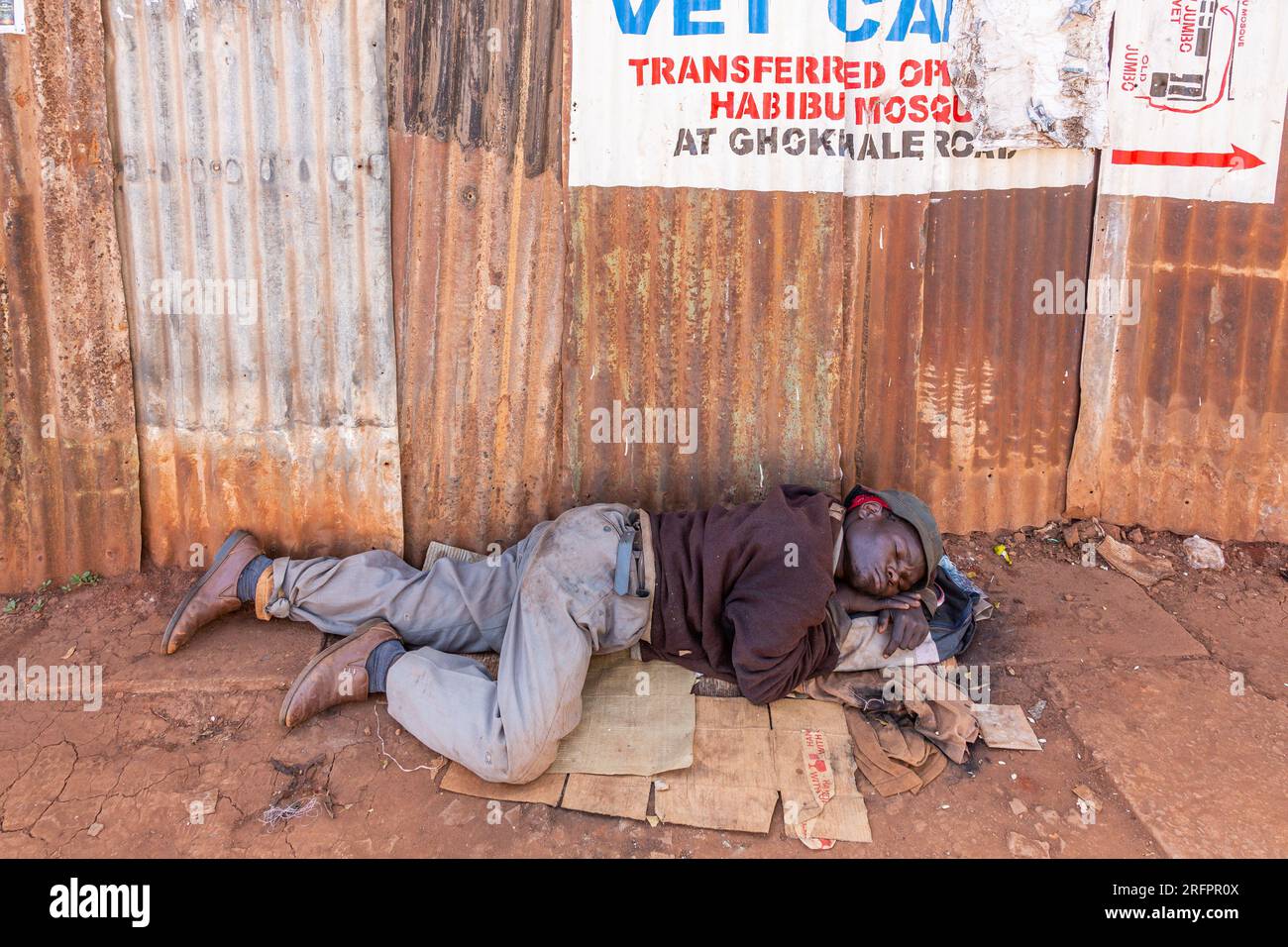 Man taking a nap, lying on some cardboard in the street. Jinja, Uganda ...