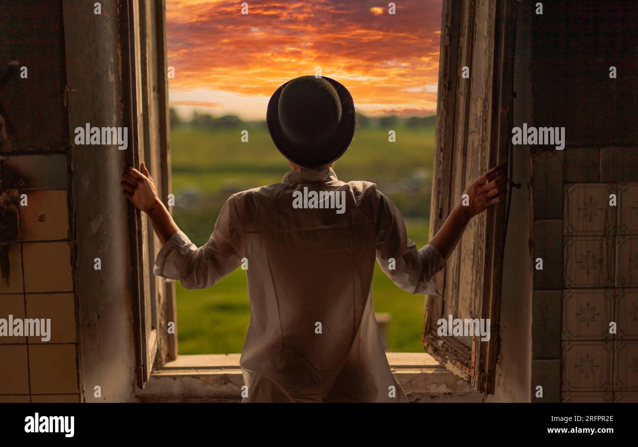 Girl with beret looks at horizon through window of a dilapidated house ...