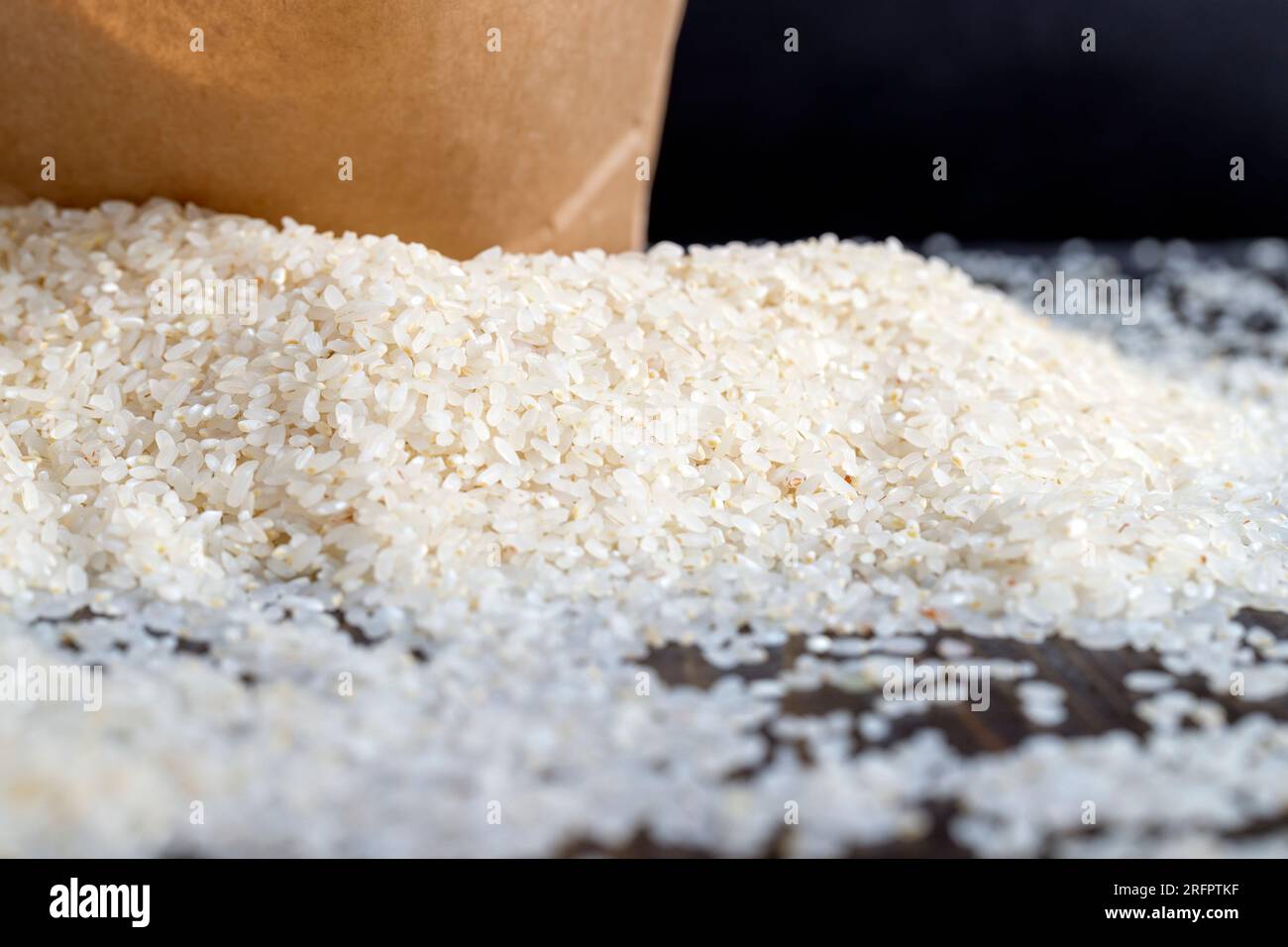 a pile of white rice in a paper bag and on the table, white uncooked ...