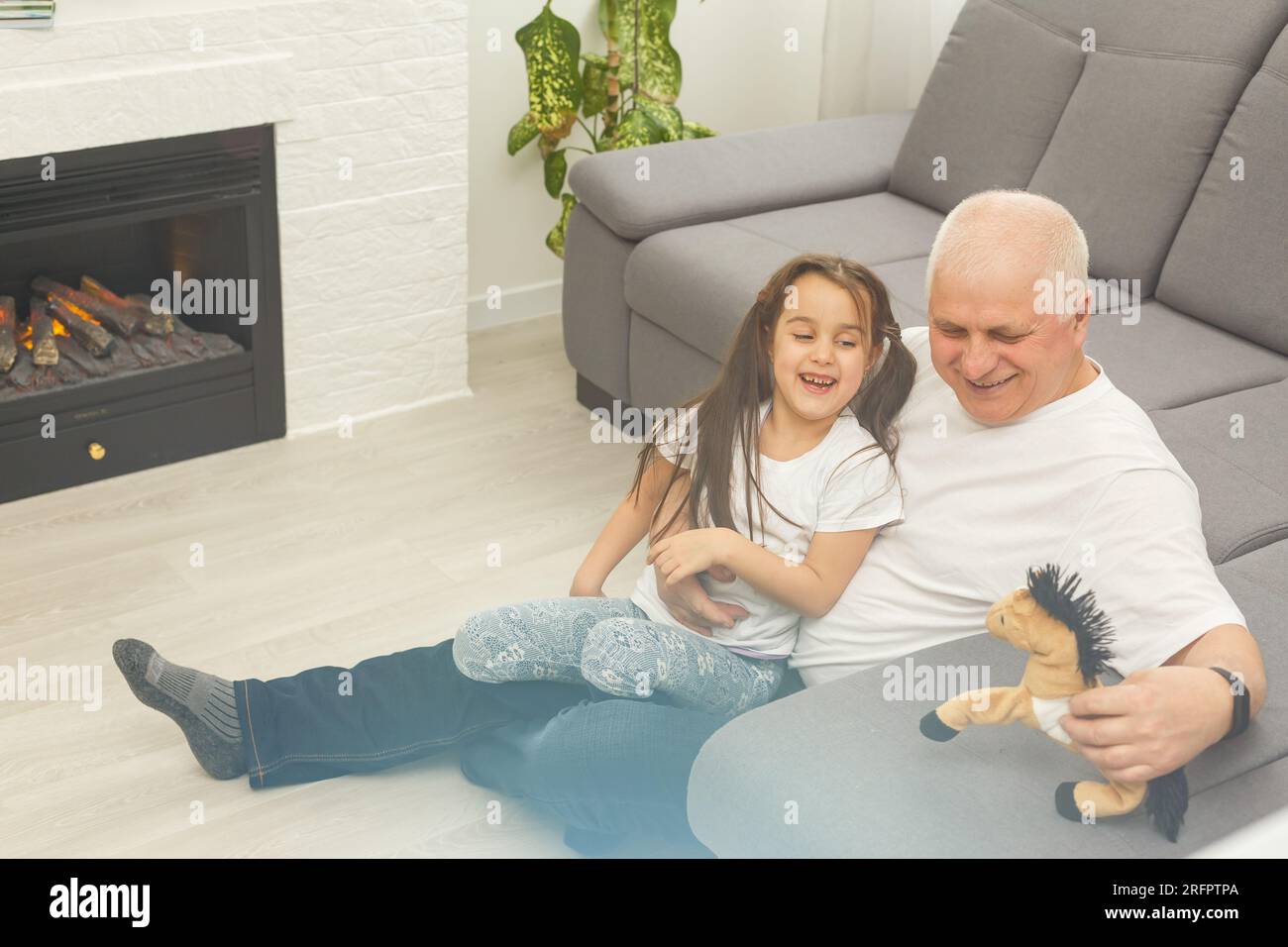 Cute little girl spending time with positive active grandpa in living ...