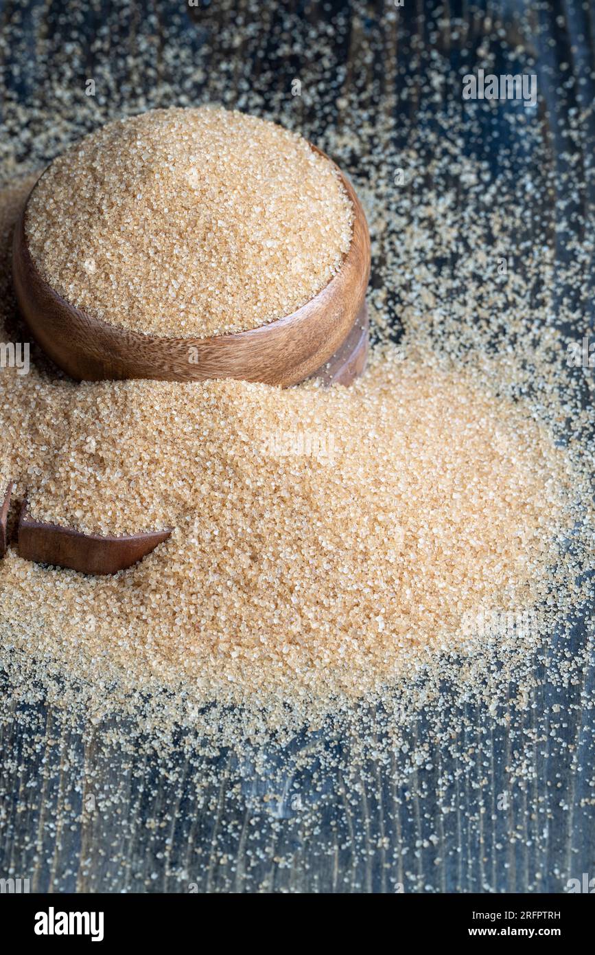 Brown crystalline sugar from cane, poured into a bowl and on the table ...