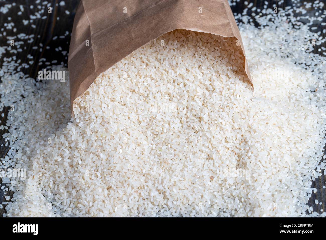 a pile of white rice in a paper bag and on the table, white uncooked ...
