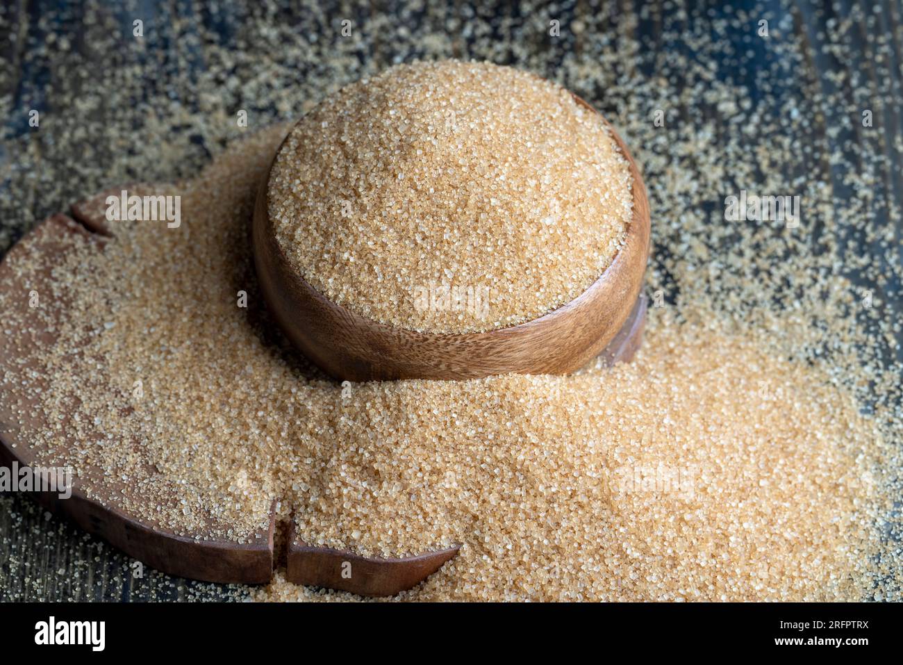 Brown crystalline sugar from cane, poured into a bowl and on the table ...