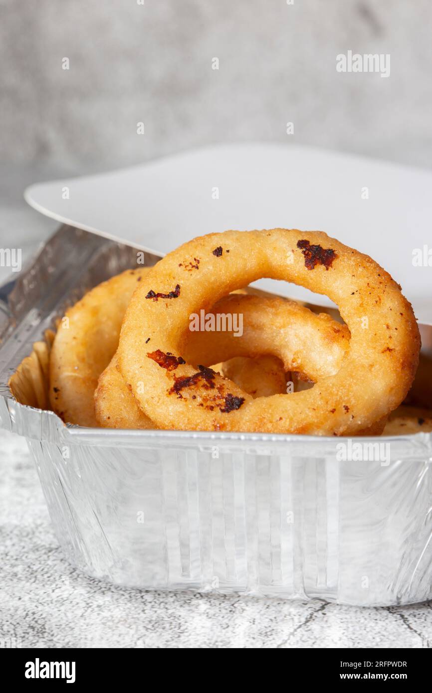 Battered onion rings in a takeaway foil tray carton container. On a ...