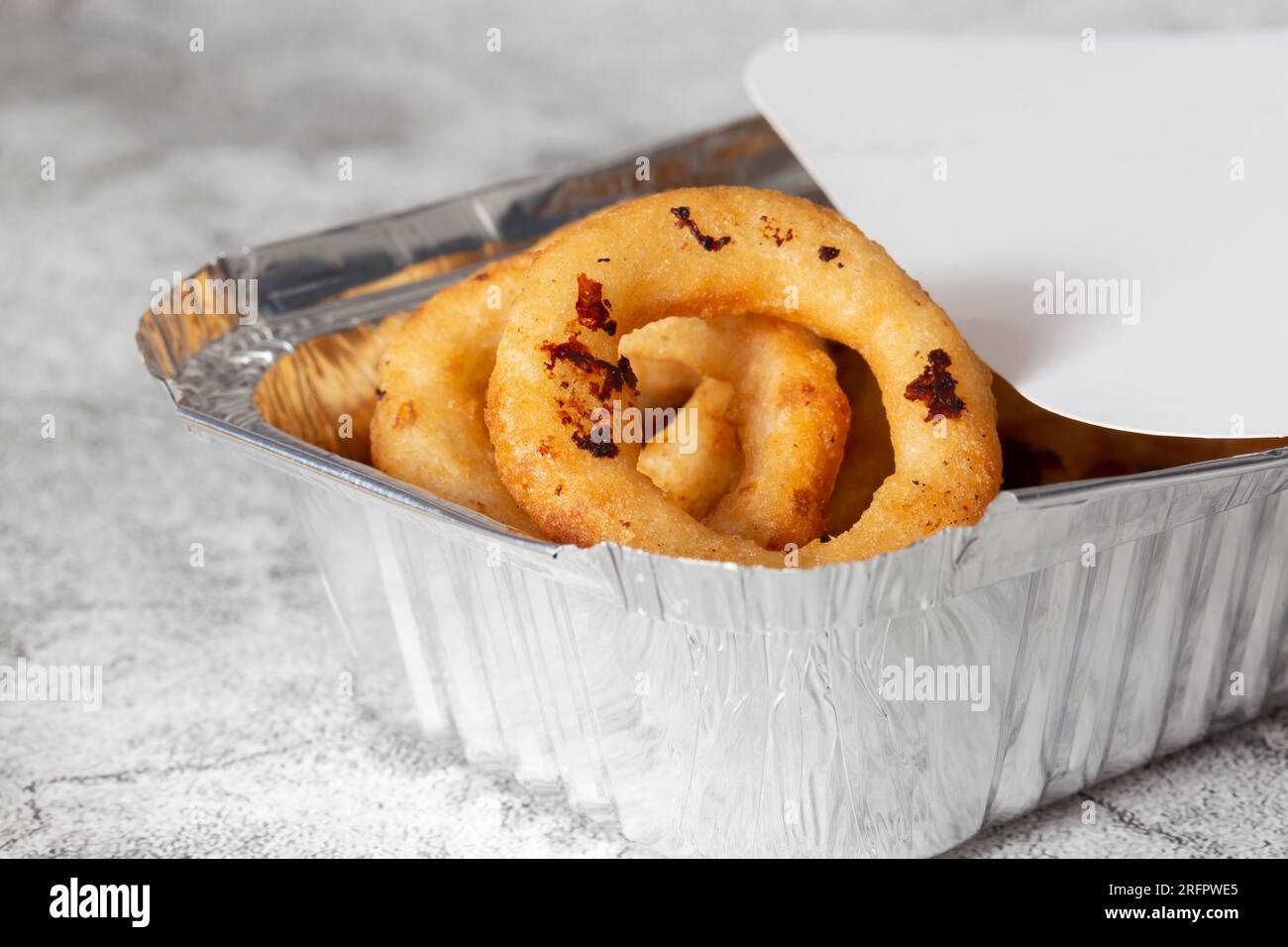 Battered onion rings in a takeaway foil tray carton container. On a ...