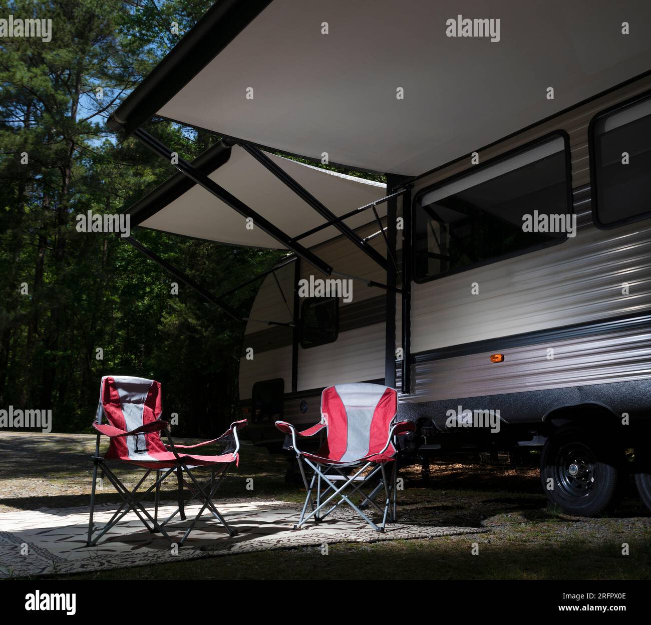 Red camping chairs that are under the awning of an RV in a campsite ...