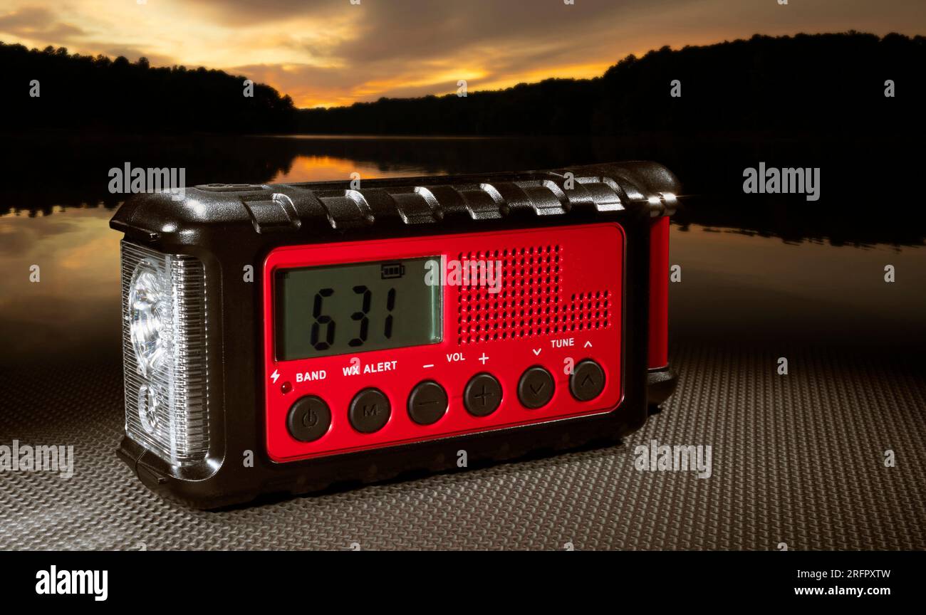 Red weather radio with clock and flashlight with the sun rising over ...