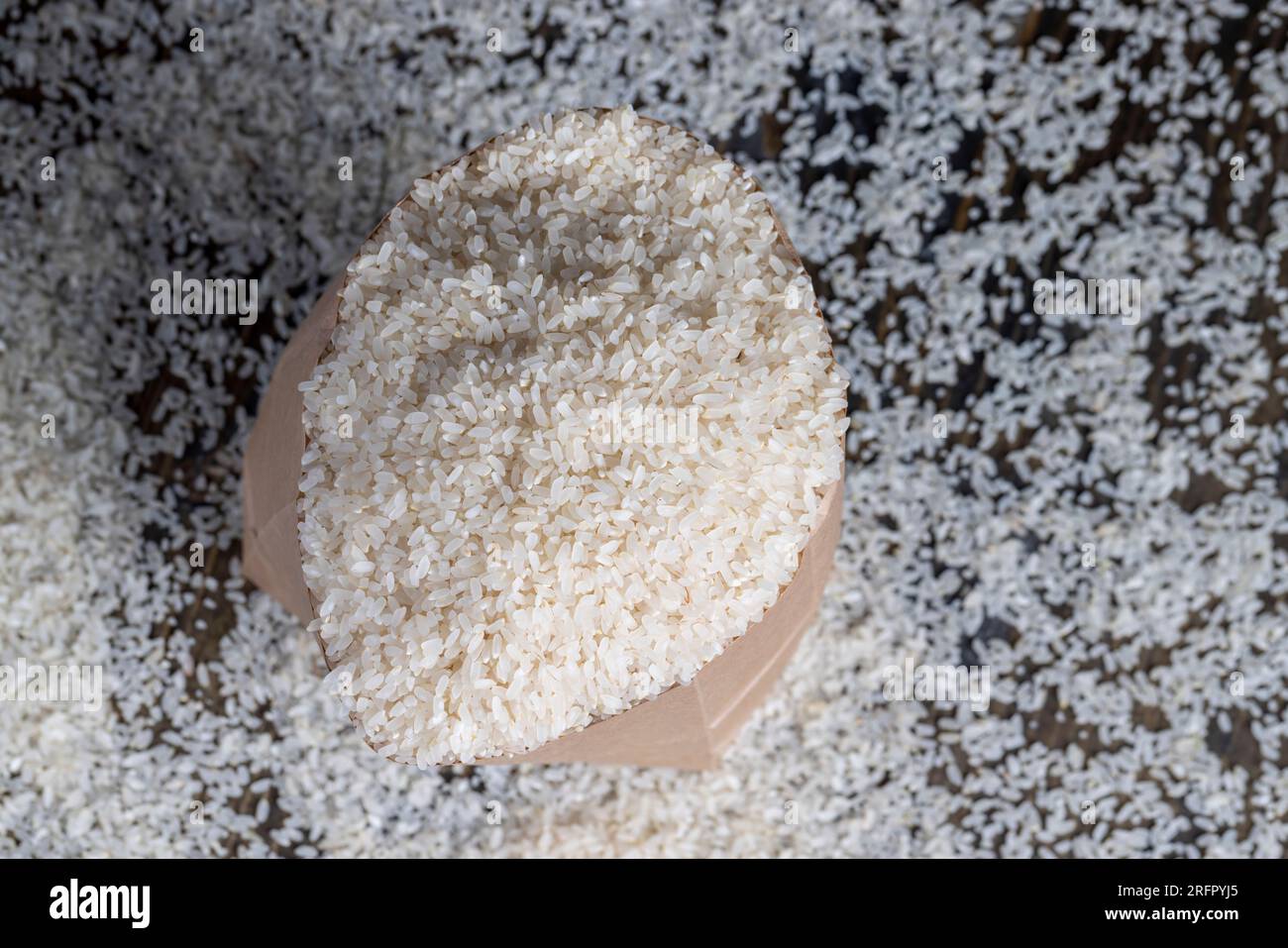 a pile of white rice in a paper bag and on the table, white uncooked ...
