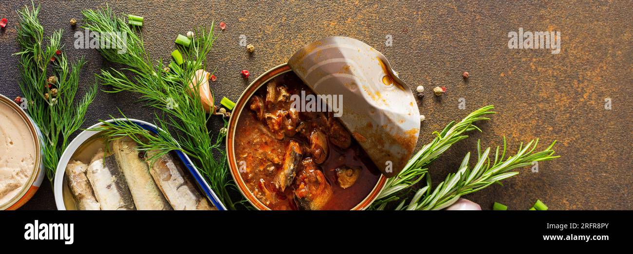 Different open tin cans with canned fish among spices and herbs banner ...