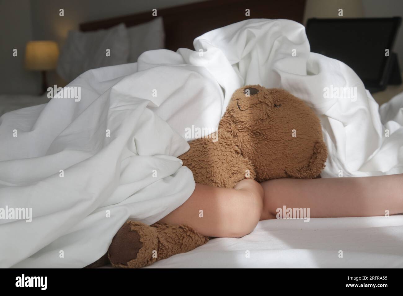 Child sleeping under white sheets hugging teddy bear. Children's nap ...