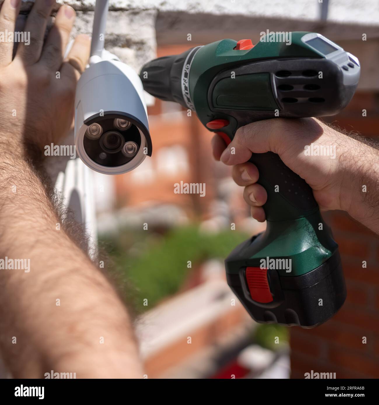 Man with a drill installing security cameras for surveillance in a ...