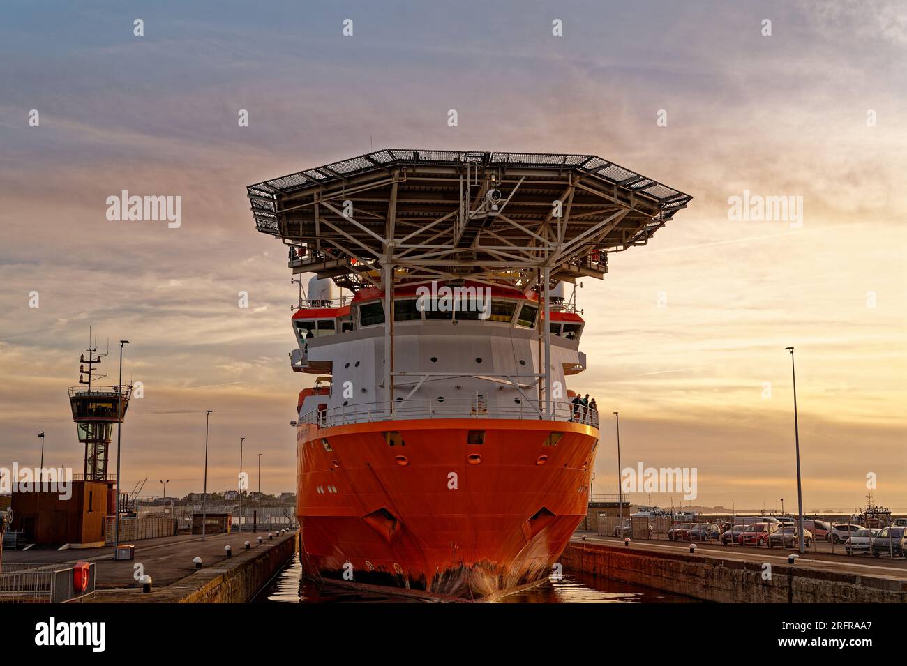 A huge merchant sea vessel in the port lock against the sky at sunset ...
