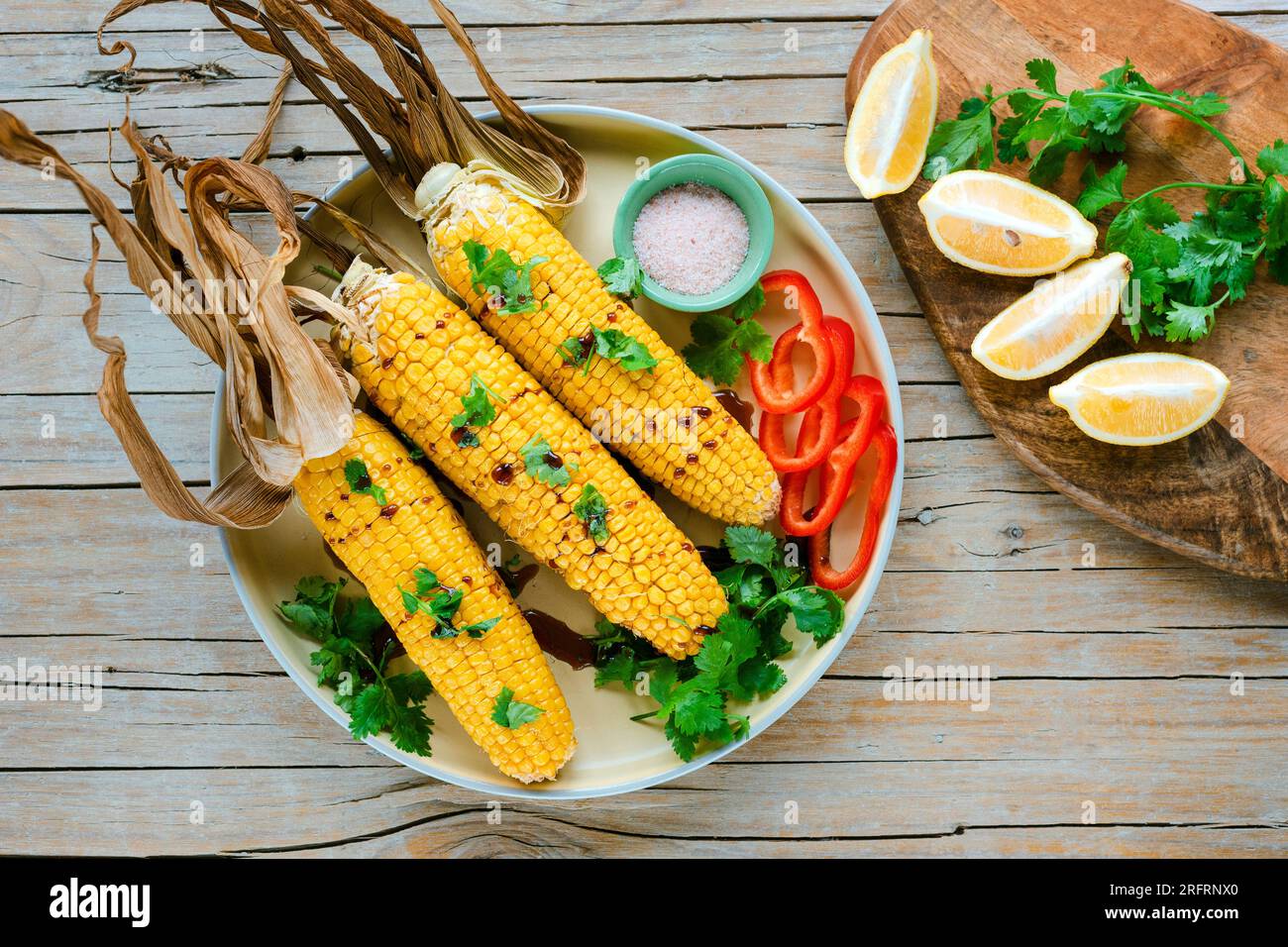 Baked corn cobs with coriander, sliced bell pepper, lemon and salt on ...