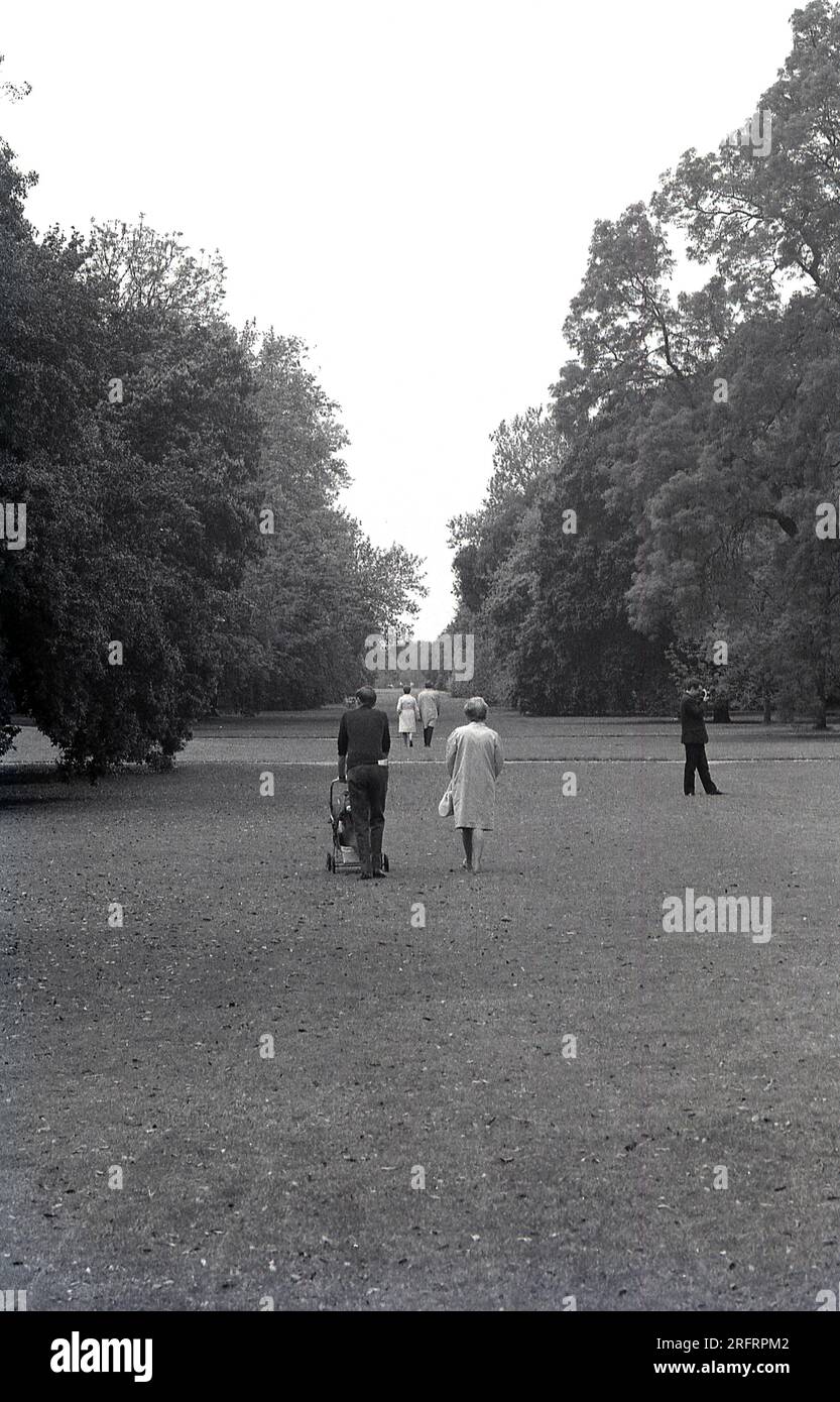 1970, historical, a couple walking on the grass in a park, the man ...