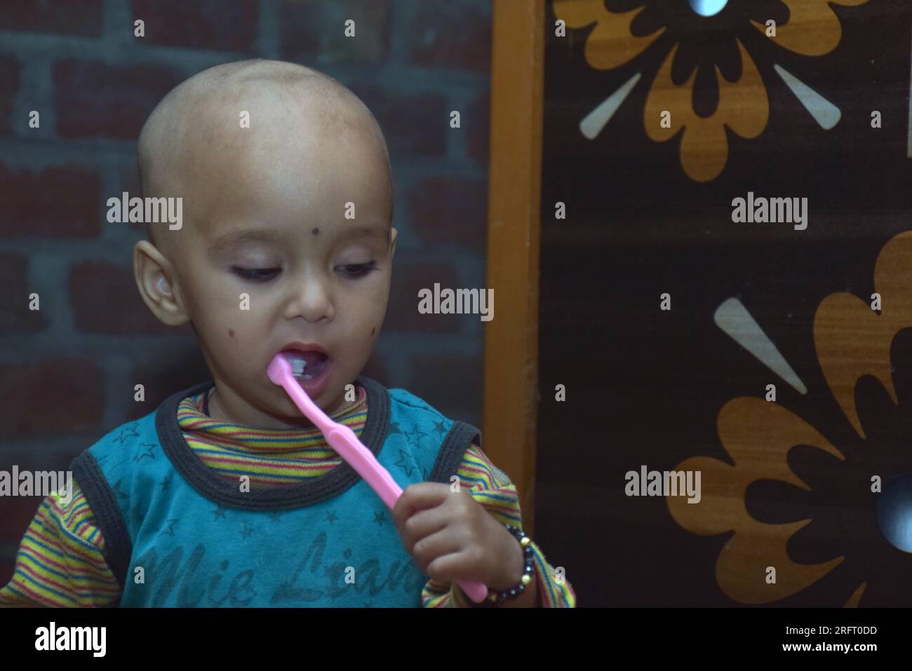 18 month old cute bald baby brushes teeth with toothbrush, brick wall ...