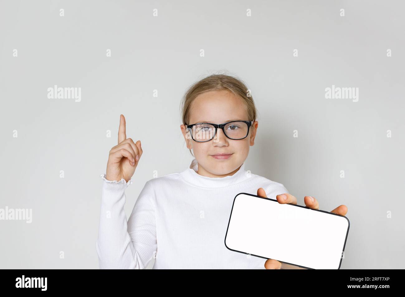 Adorable child girl with smartphone pointing up on white background ...