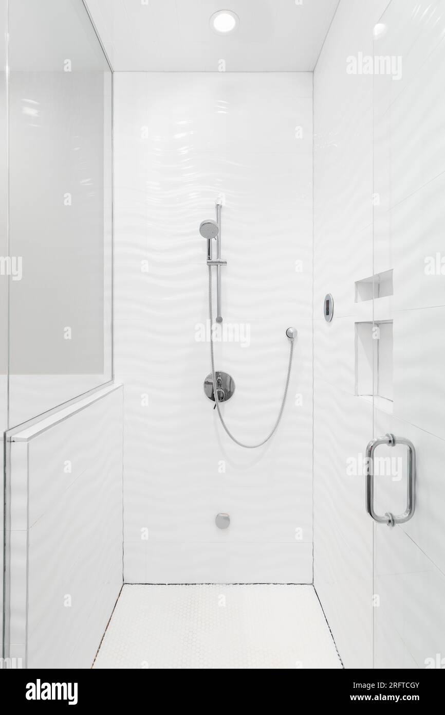 A walk-in shower with white wavy tiles on the walls, chrome faucet, and ...