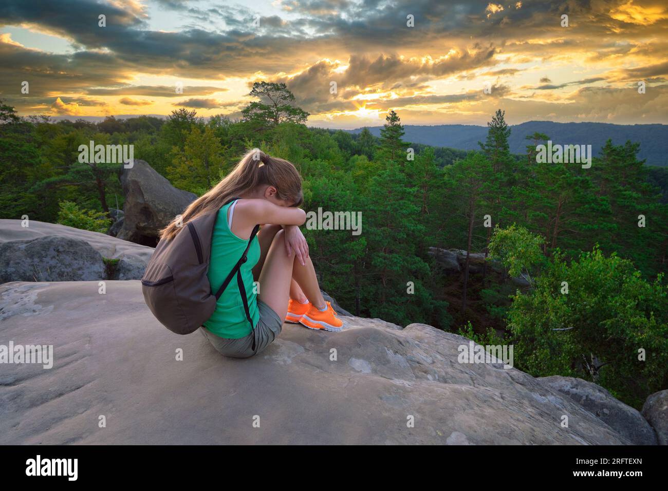 Lonely young woman sitting depressed on hillside trail on warm summer ...