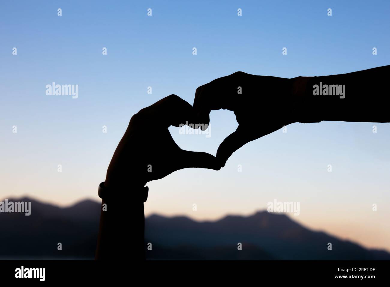 silhouette of hands in the shape of a heart against a beautiful ...