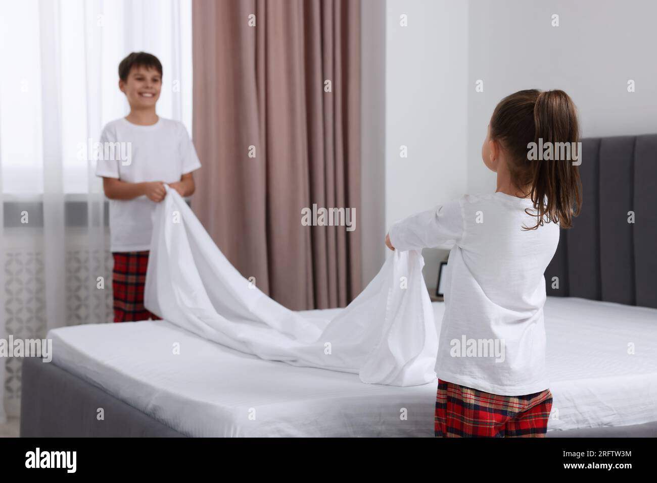 Brother and sister changing bed linens together in bedroom Stock Photo ...