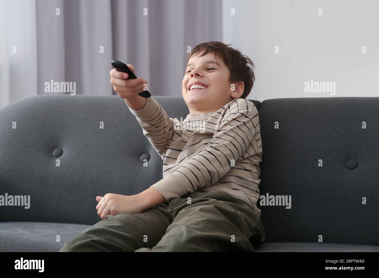 Happy boy changing TV channels with remote control on sofa at home ...