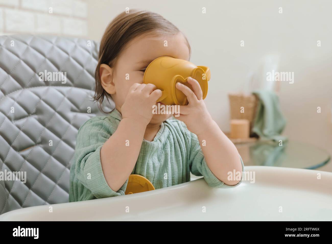 Cute little baby drinking from cup in high chair indoors Stock Photo ...