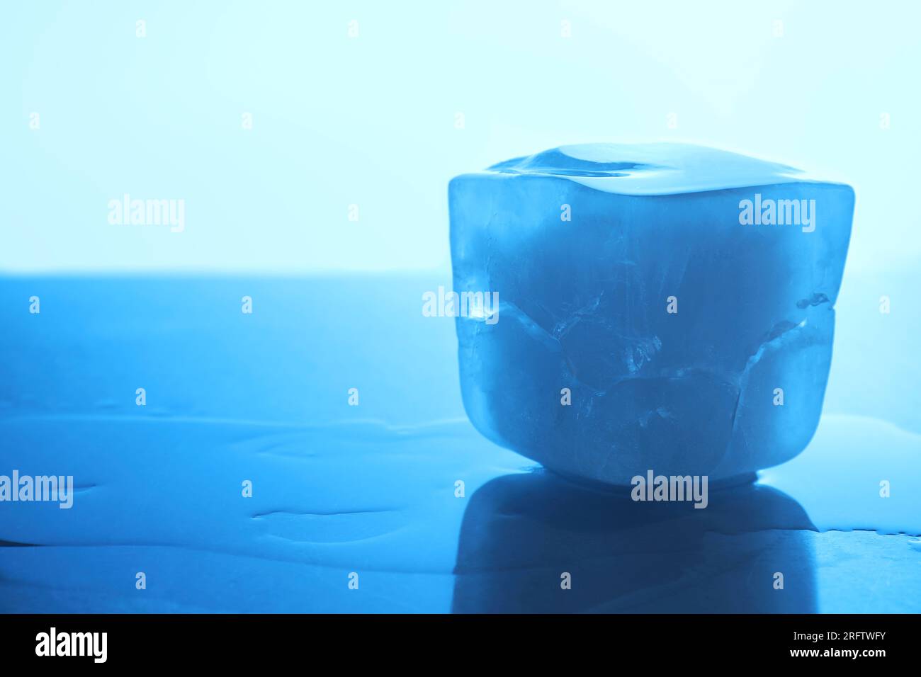 One crystal clear ice cube on light blue background, closeup and space for text. Color tone ...