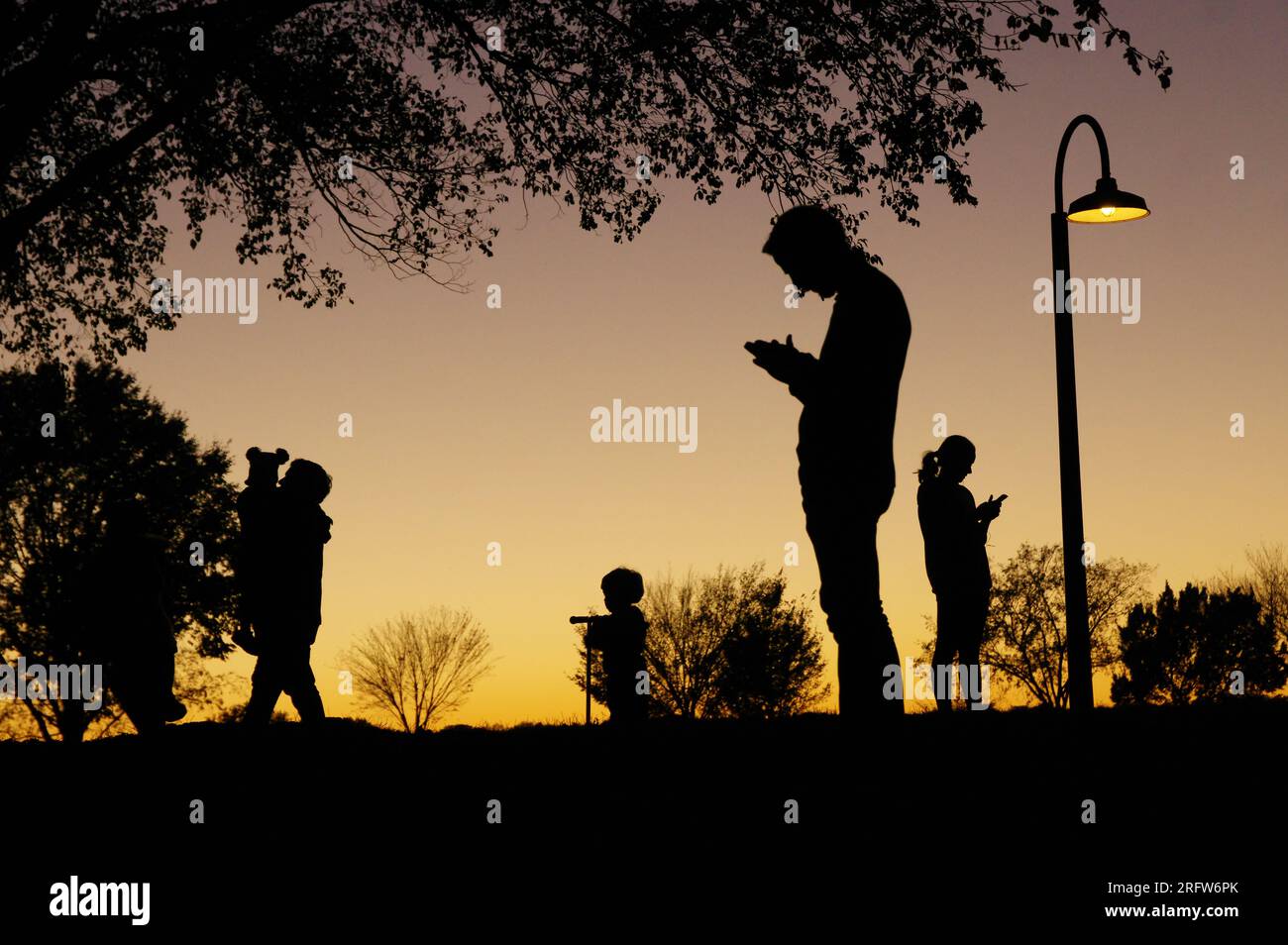 A scene at dusk: silhouettes of people walking, using their cell phones ...
