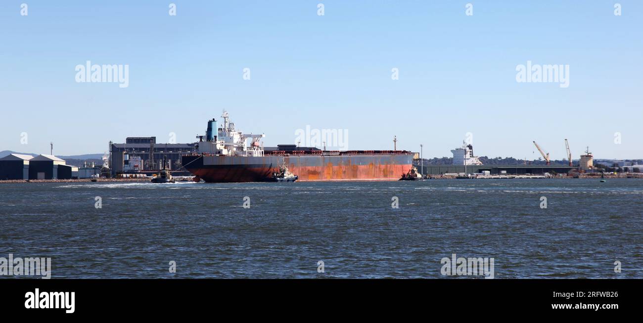 Large coal carrying ship being brought into harbour by tug boats ...