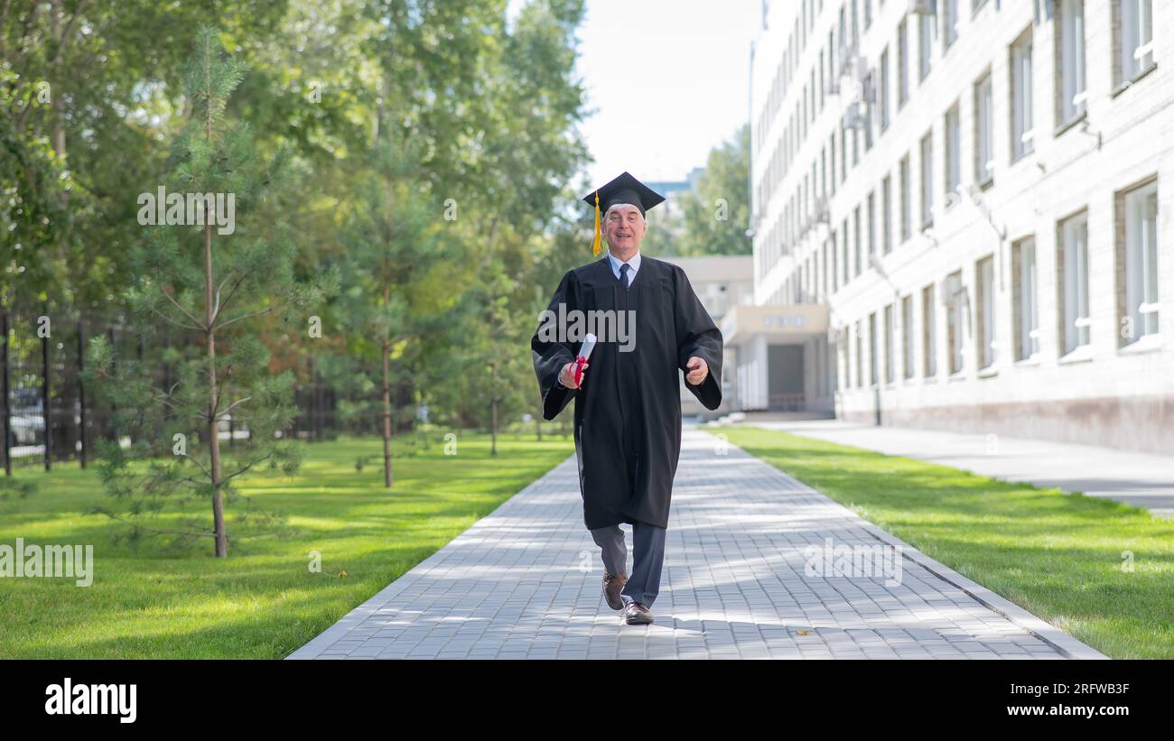 An old man in a graduation gown walks outdoors and holds a diploma ...