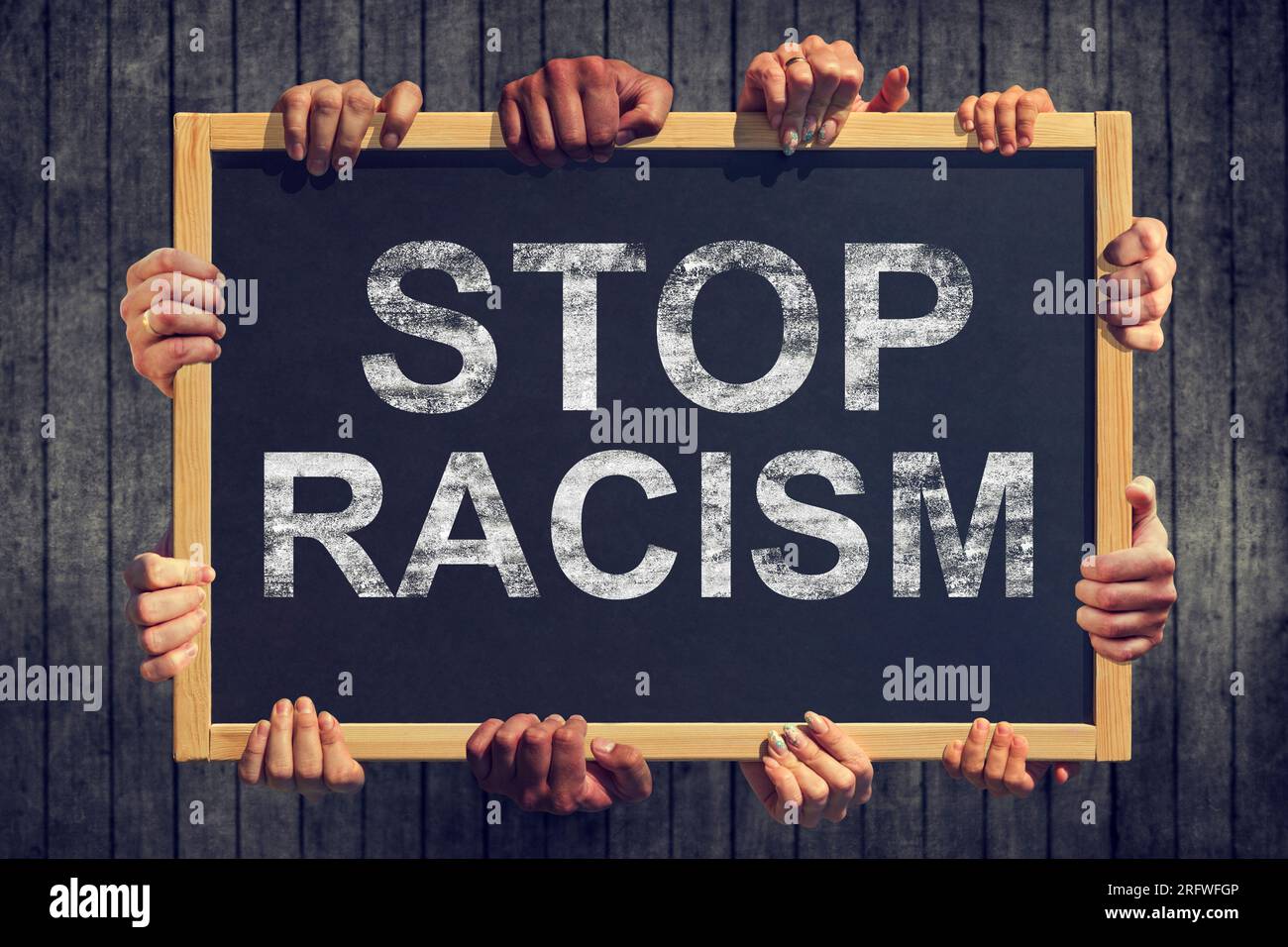 A lot of hand are holding a banner with text " Stop racism" on dark ...