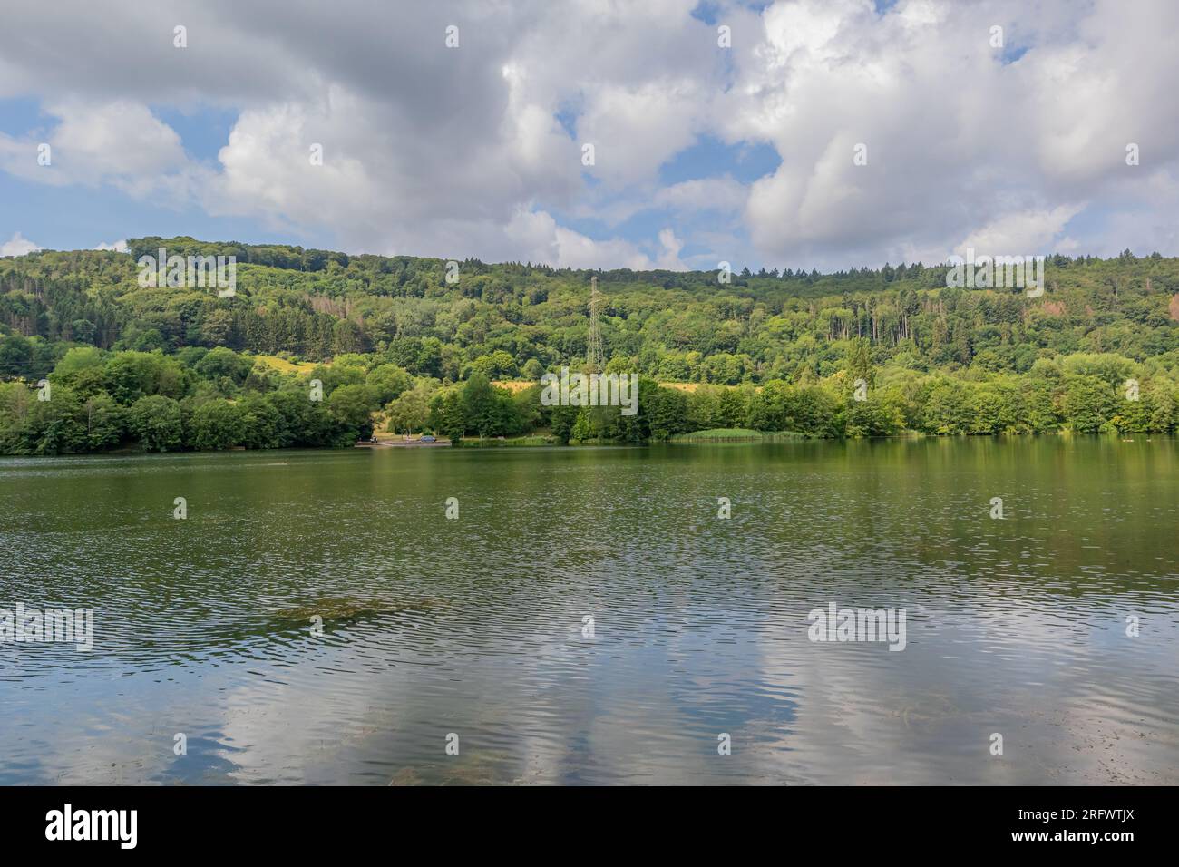 Lake Echternach with its calm water, hills with abundant leafy trees in ...
