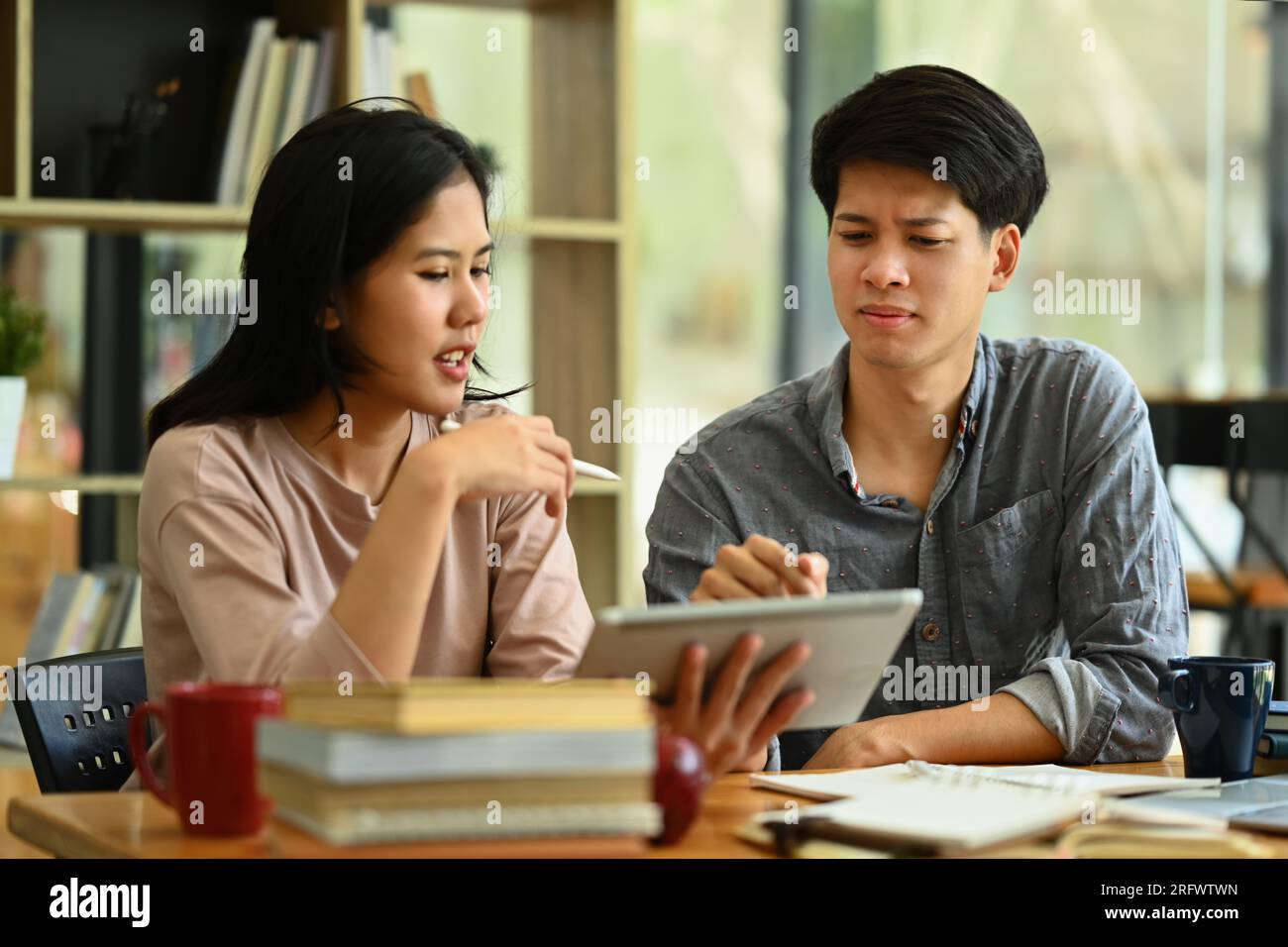 Two friendly university student sitting at table with laptop, talking ...