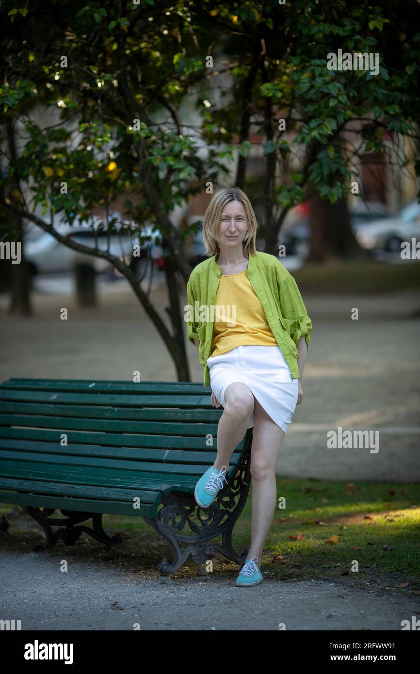 A woman in a skirt sits on a park bench Stock Photo - Alamy