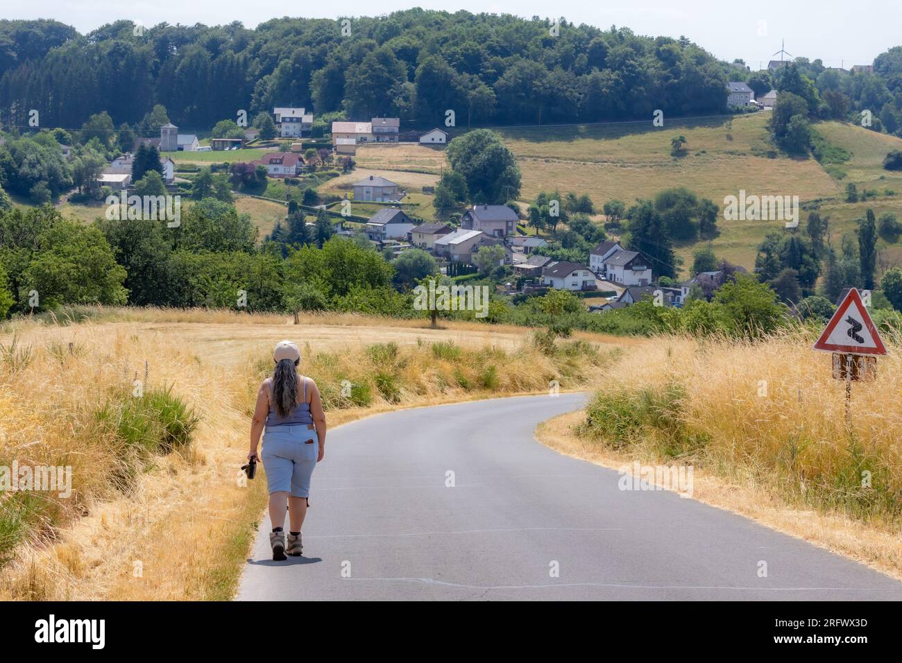 Country asphalt road with adult female hiker walking on left side ...
