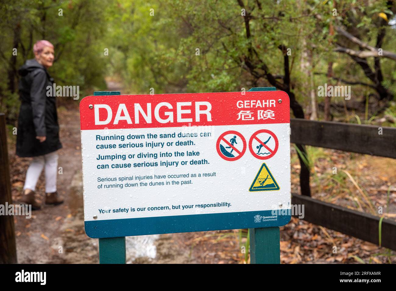 Fraser Island woman walks by Danger sign on trail to Lake Wabby warning ...