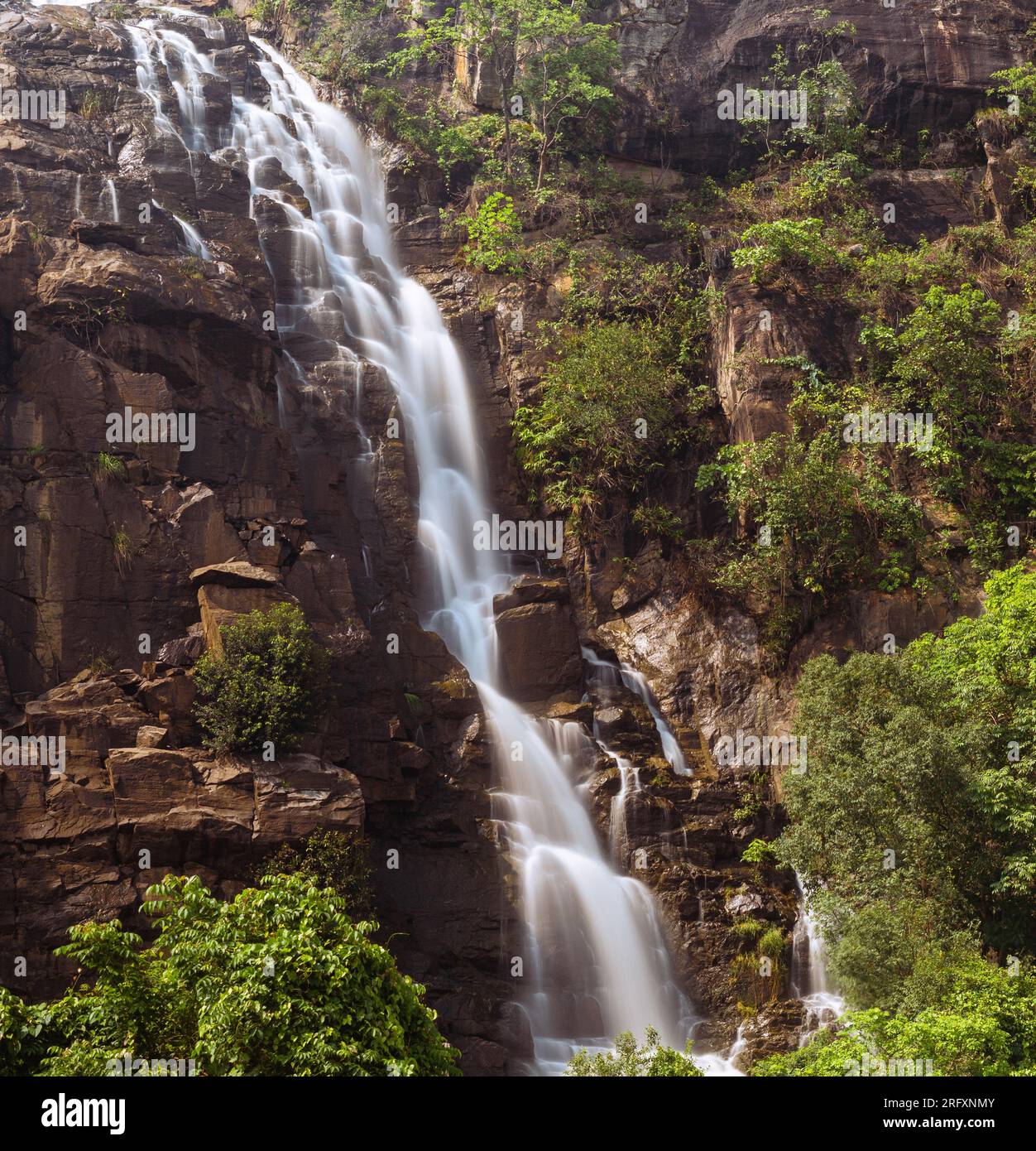 Silky milky smooth Sita waterfall flowing over green rocky hills at ...