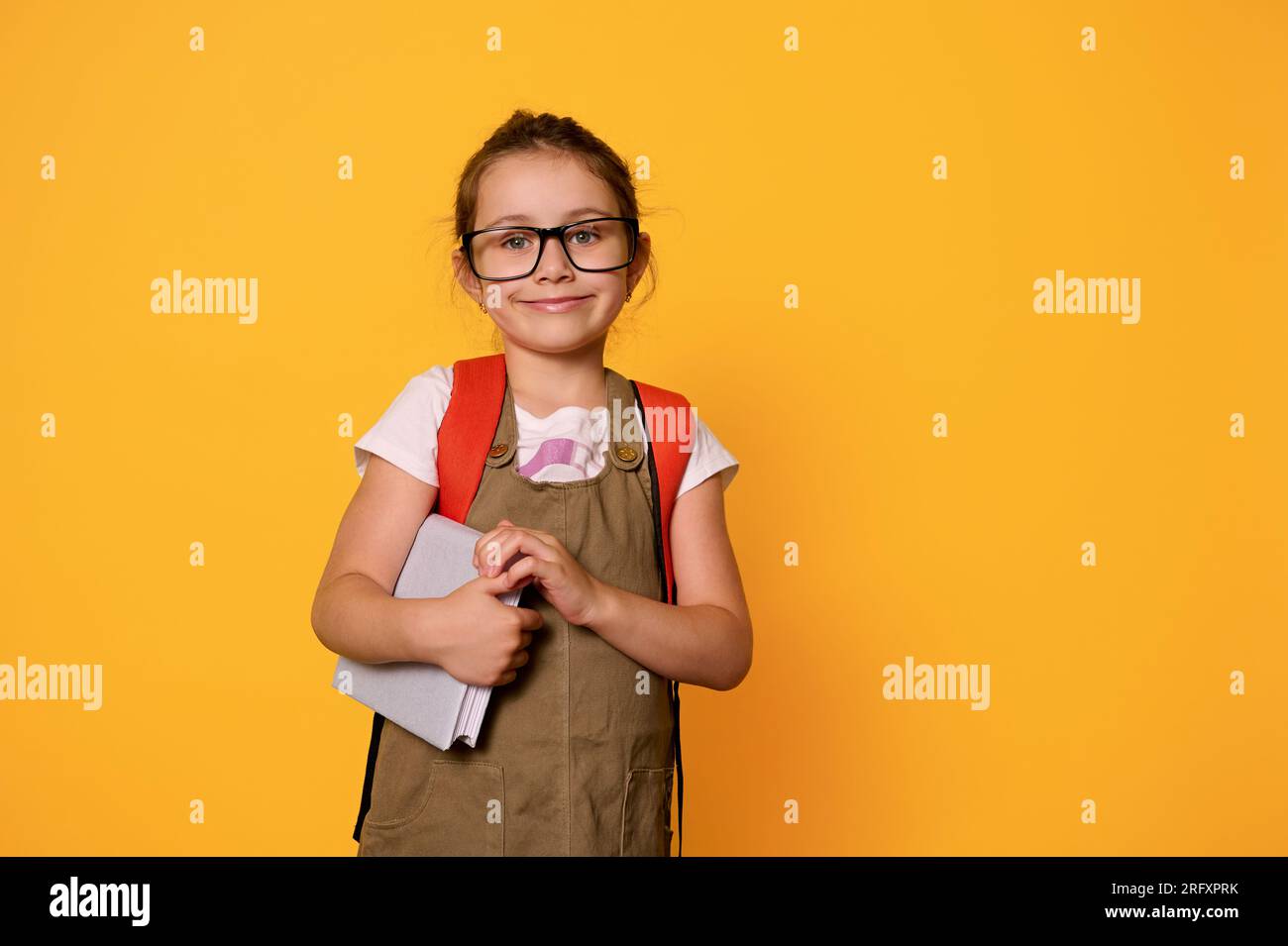 Advertising studio portrait of Caucasian chappy smiling elementary age school girl with backpack ...