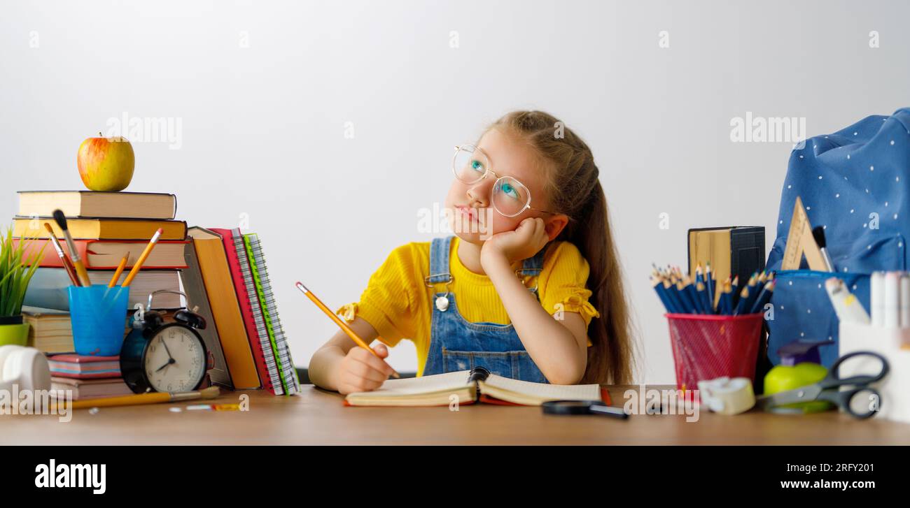 Back to school. Thinking child is sitting at desk. Girl doing homework ...