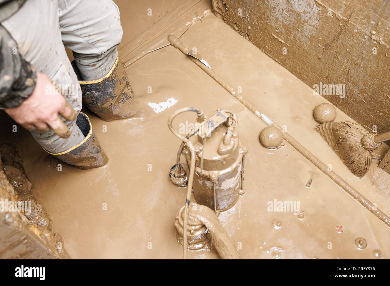 A man stands in ankle-deep mud in the basement while cleaning his flood ...
