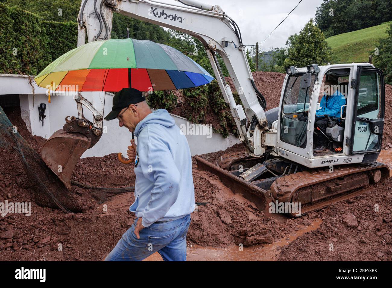 A man walks past a digger that is cleaning a thick layer of debris in ...