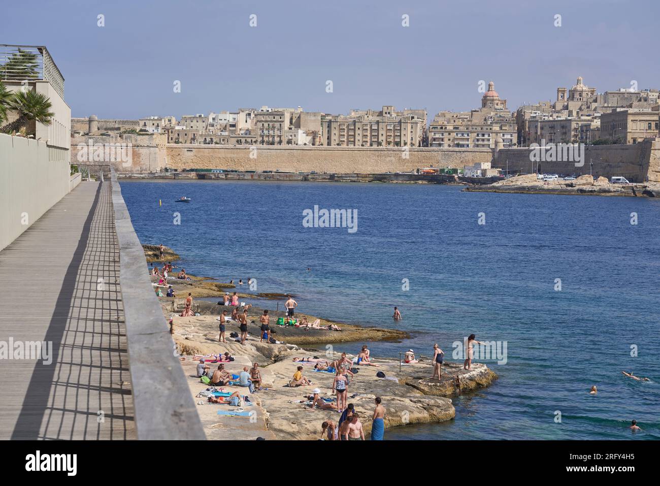 Rocky coast line of the city of Sliema in Malta. People relaxing on the ...