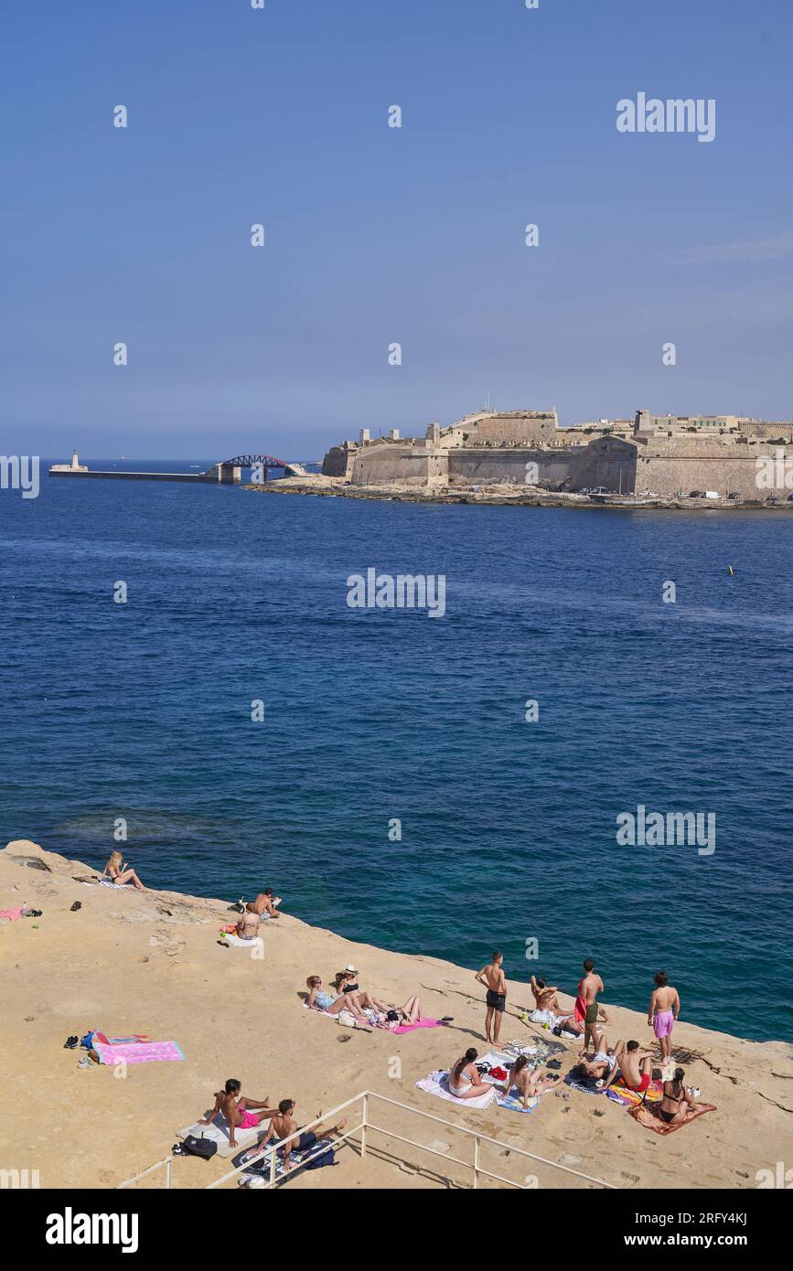 Rocky coast line of the city of Sliema in Malta. People relaxing on the ...