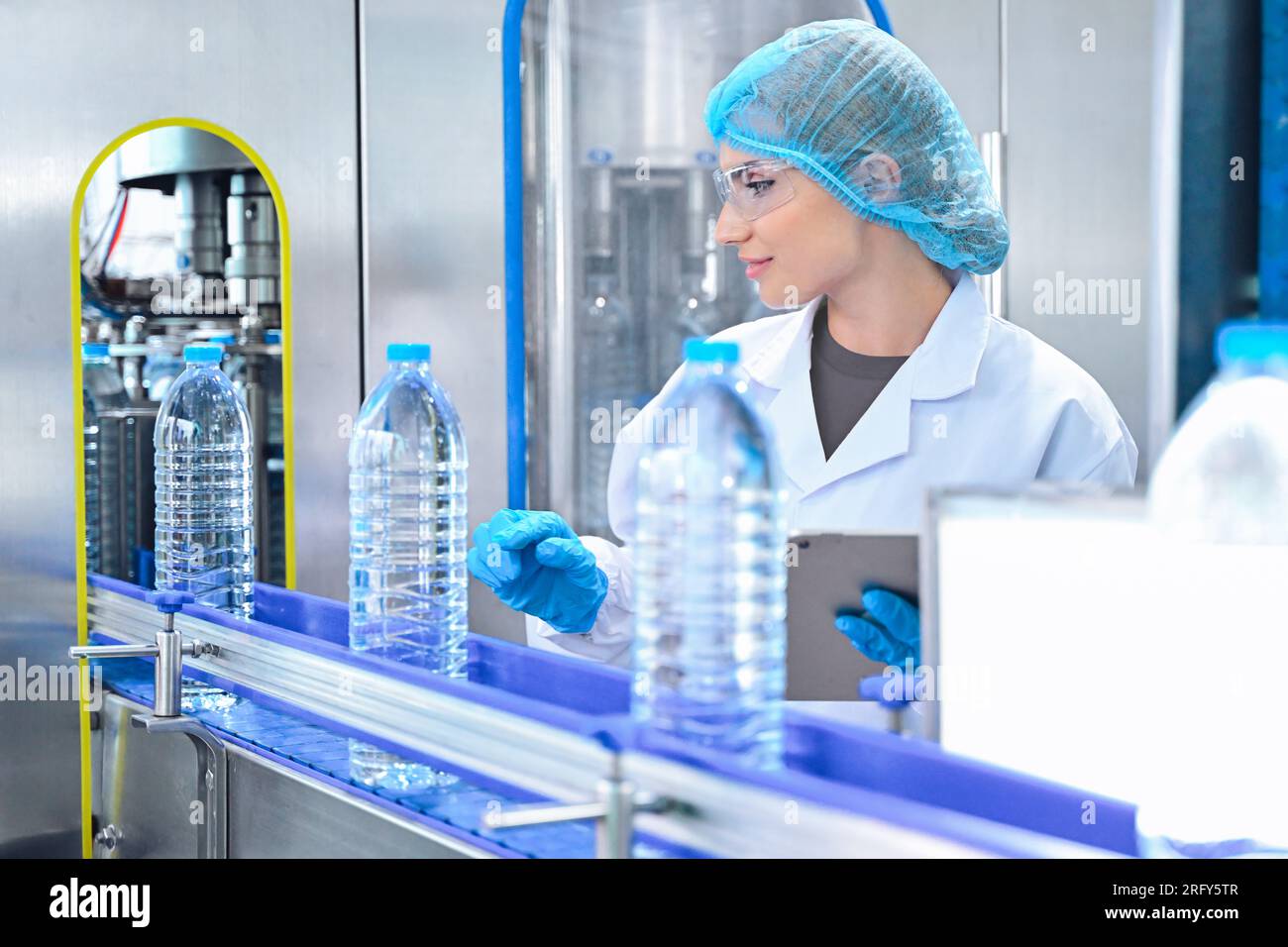 Bottling factory worker inspecting quality of water bottles before ...