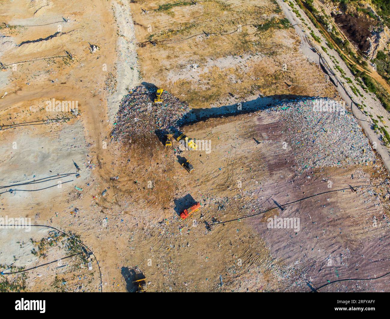 Aerial view from above of dumping site. Garbage trucks. Yellow tractor ...
