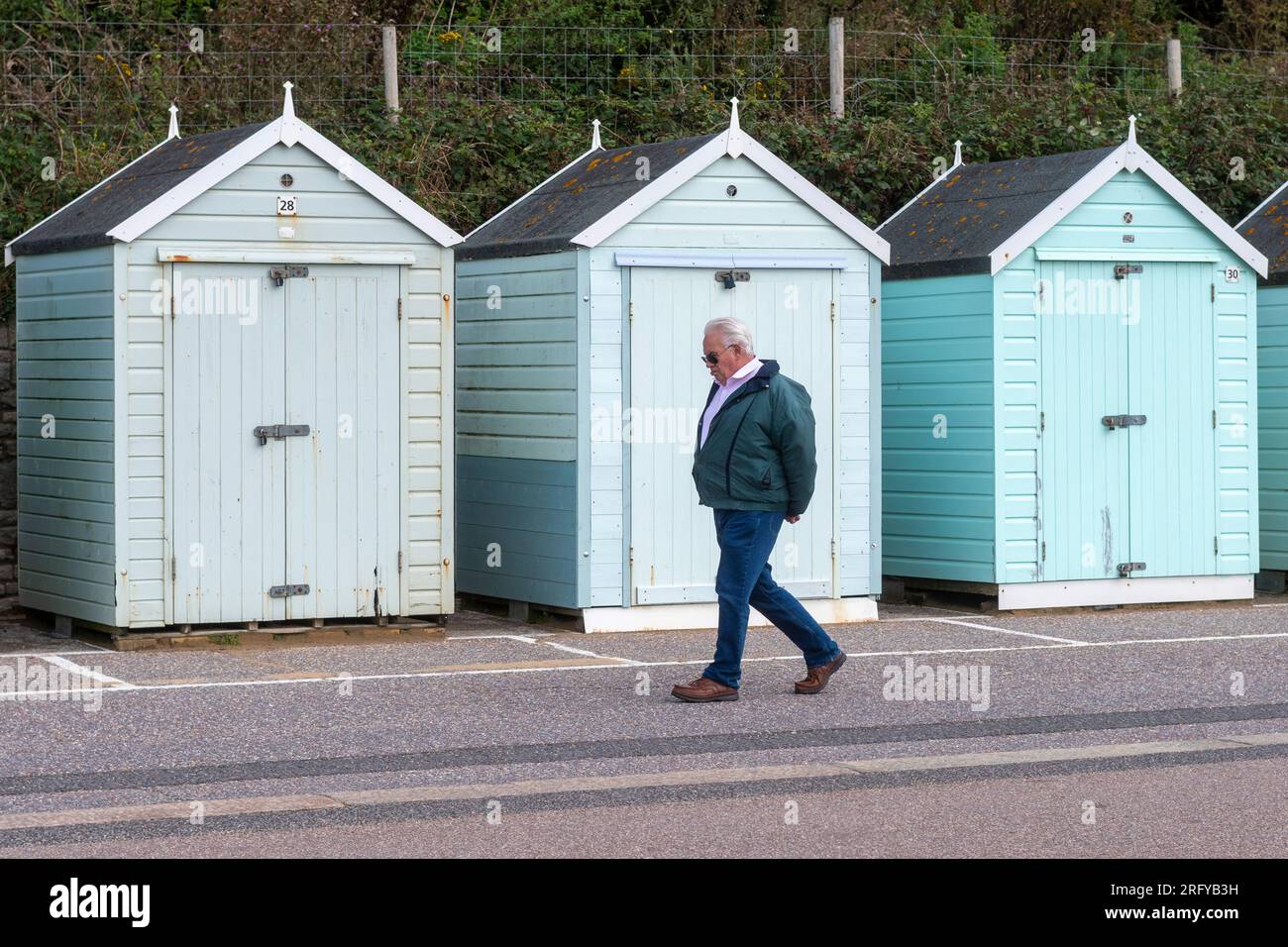 Man walking into wind past blue beach huts on the seafront, Bournemouth ...