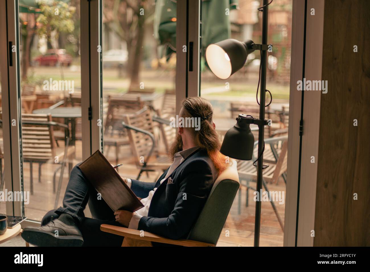 Handsome bearded man writing something on his notepad with his legs ...