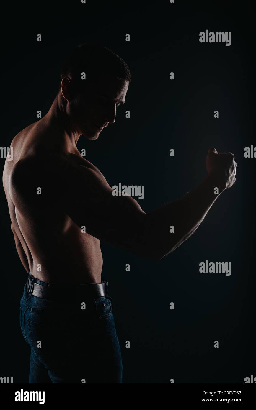 Muscular and good-looking man standing in a dark room and flexing his ...
