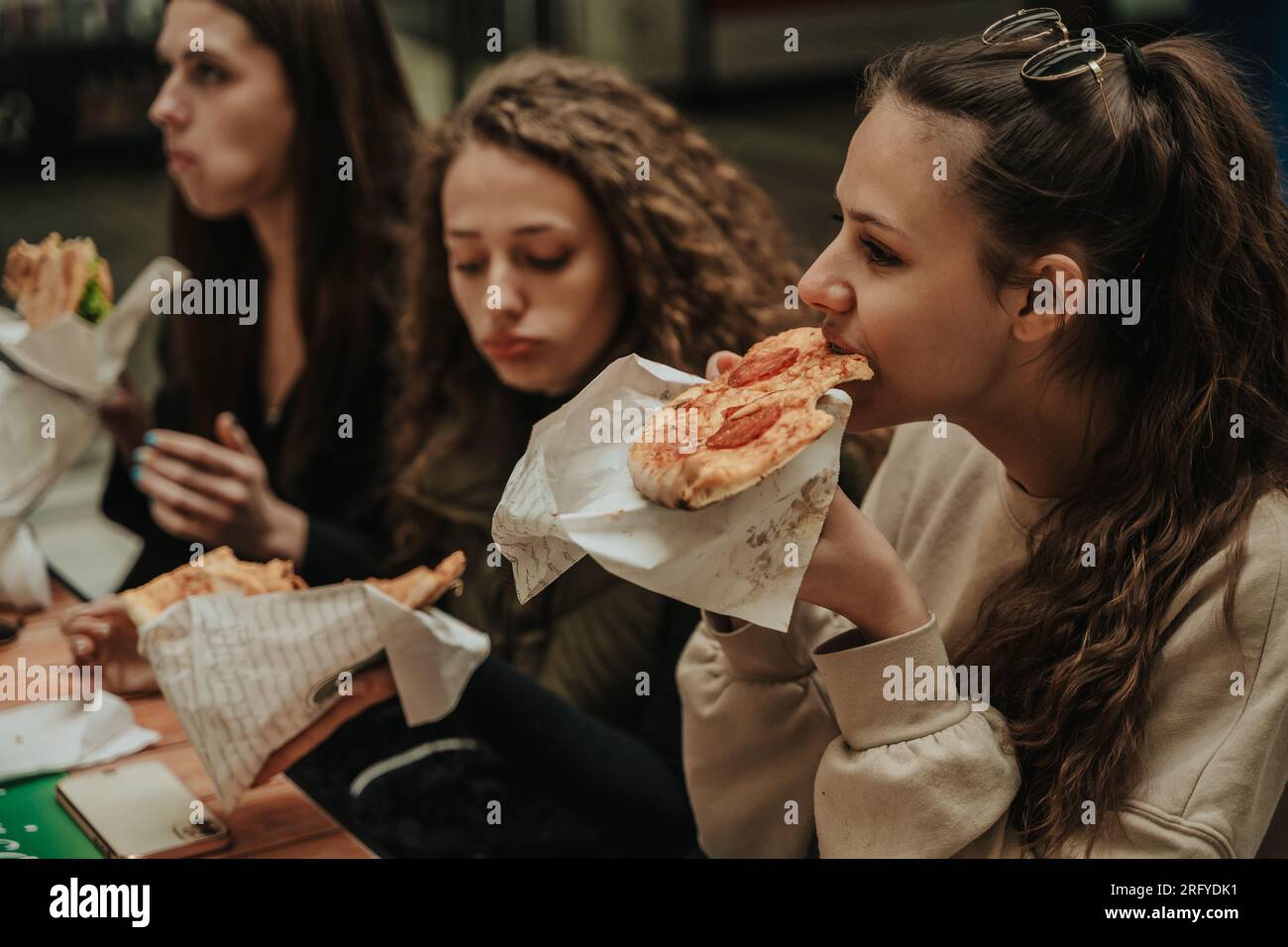 Gorgeous girls eating a pizza. Brunette girl biting her slice. Close up ...
