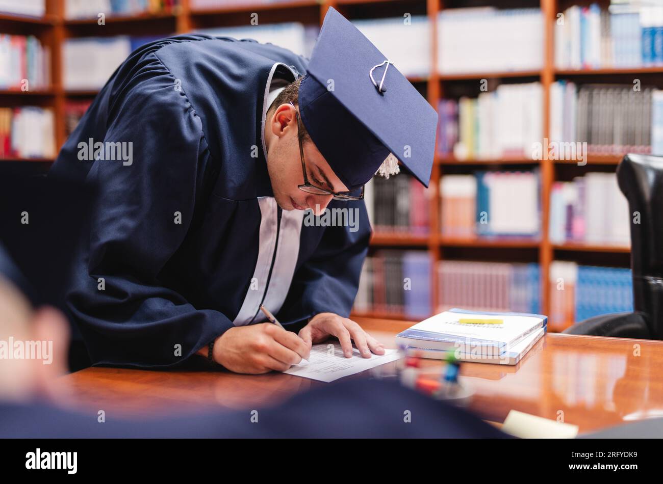 Young male graduate writing his personal information and signature on ...